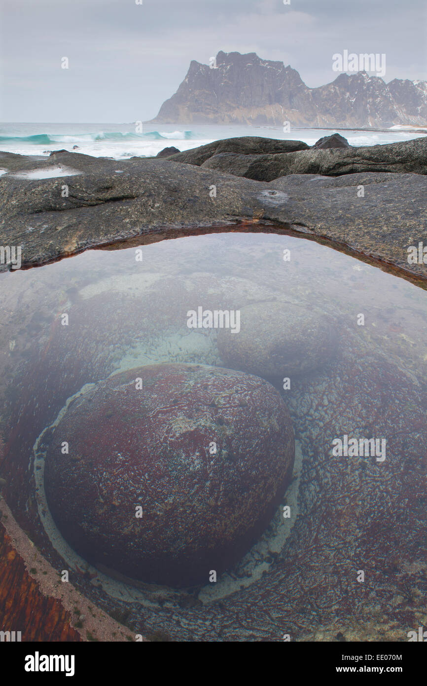Coastal scene with rock pool and boulder in foreground and mountains in ...