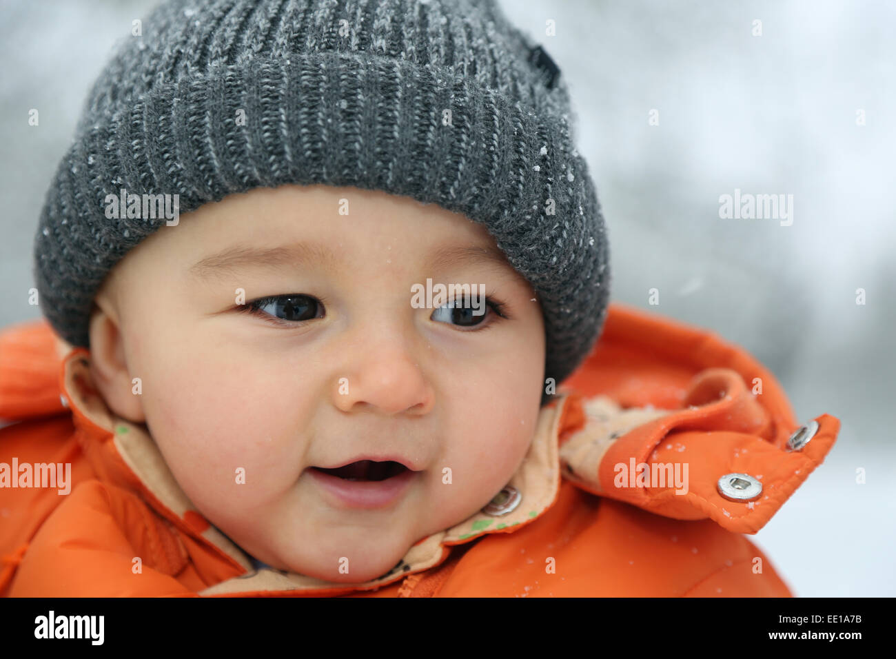 Portrait of a happy baby with snow in winter with cap and warm clothing ...