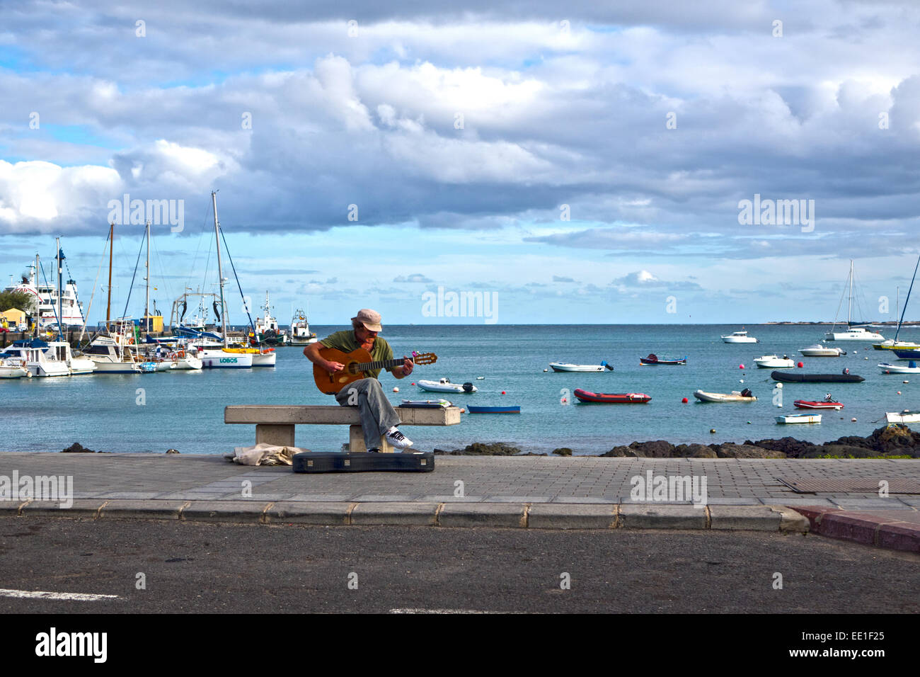Man playing guitar on a bench by the harbor harbour in Corralejo Canary ...
