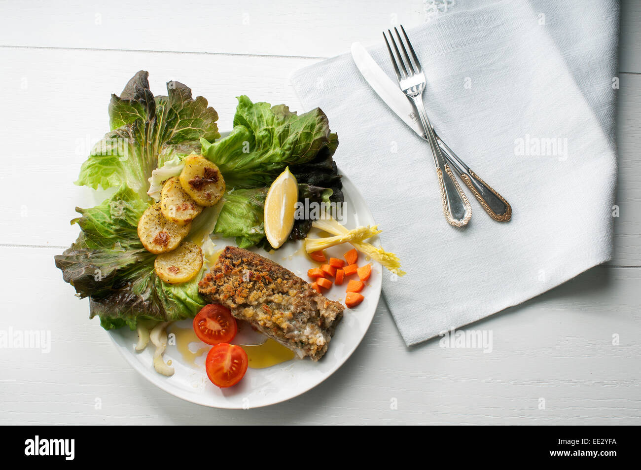 cod fillet breaded and baked with potatoes and salad as garnishing ...