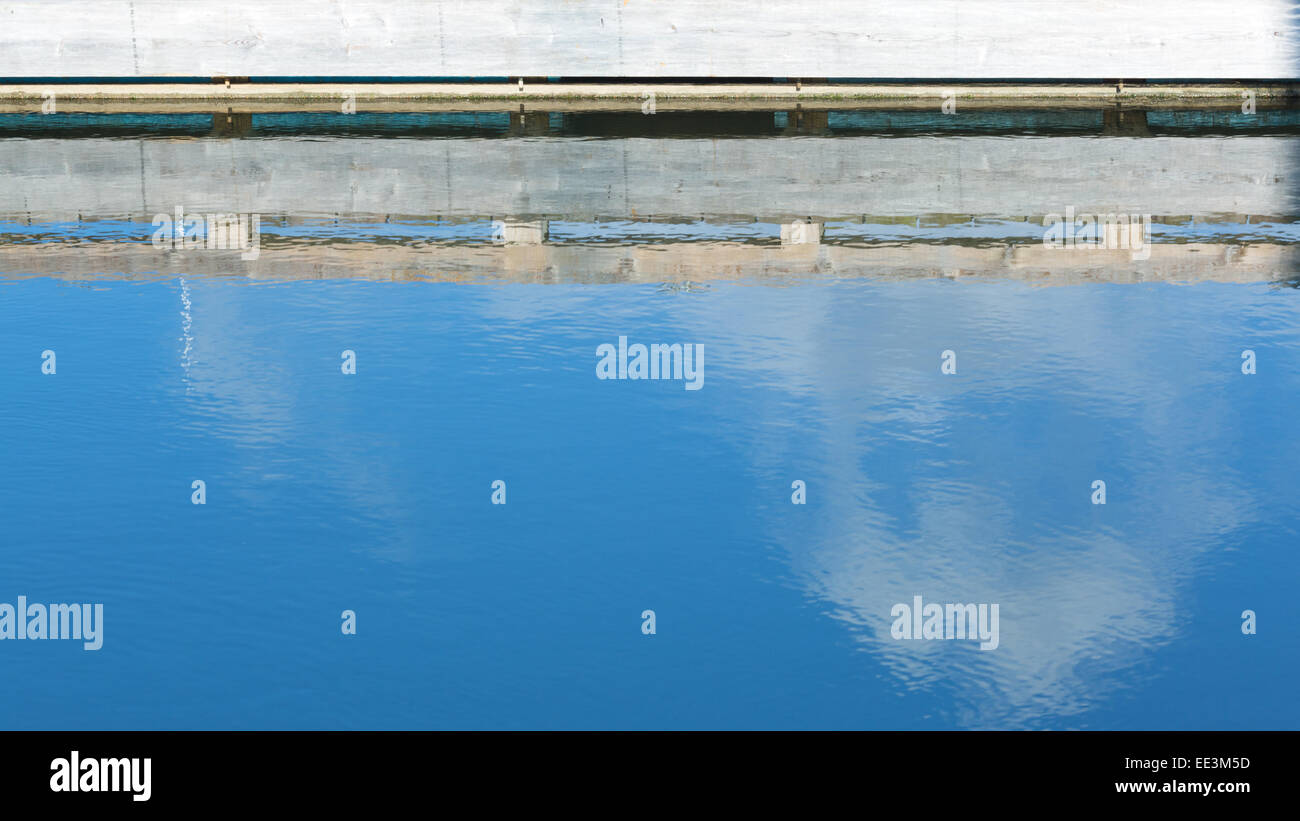 The blurred reflection of a floating wharf with clouds against a blue ...