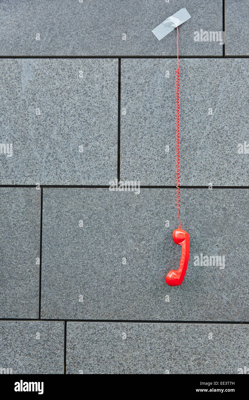 Red phone hanging down taped to a grey wall Stock Photo - Alamy
