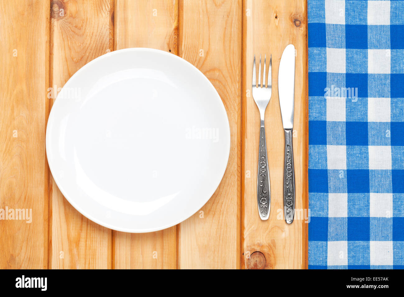 Empty plate, silverware and towel over wooden table background. View ...