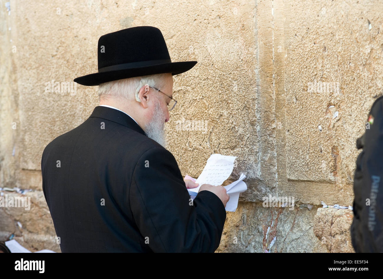 A jewish man is reading from a paper in front of the western wall in ...