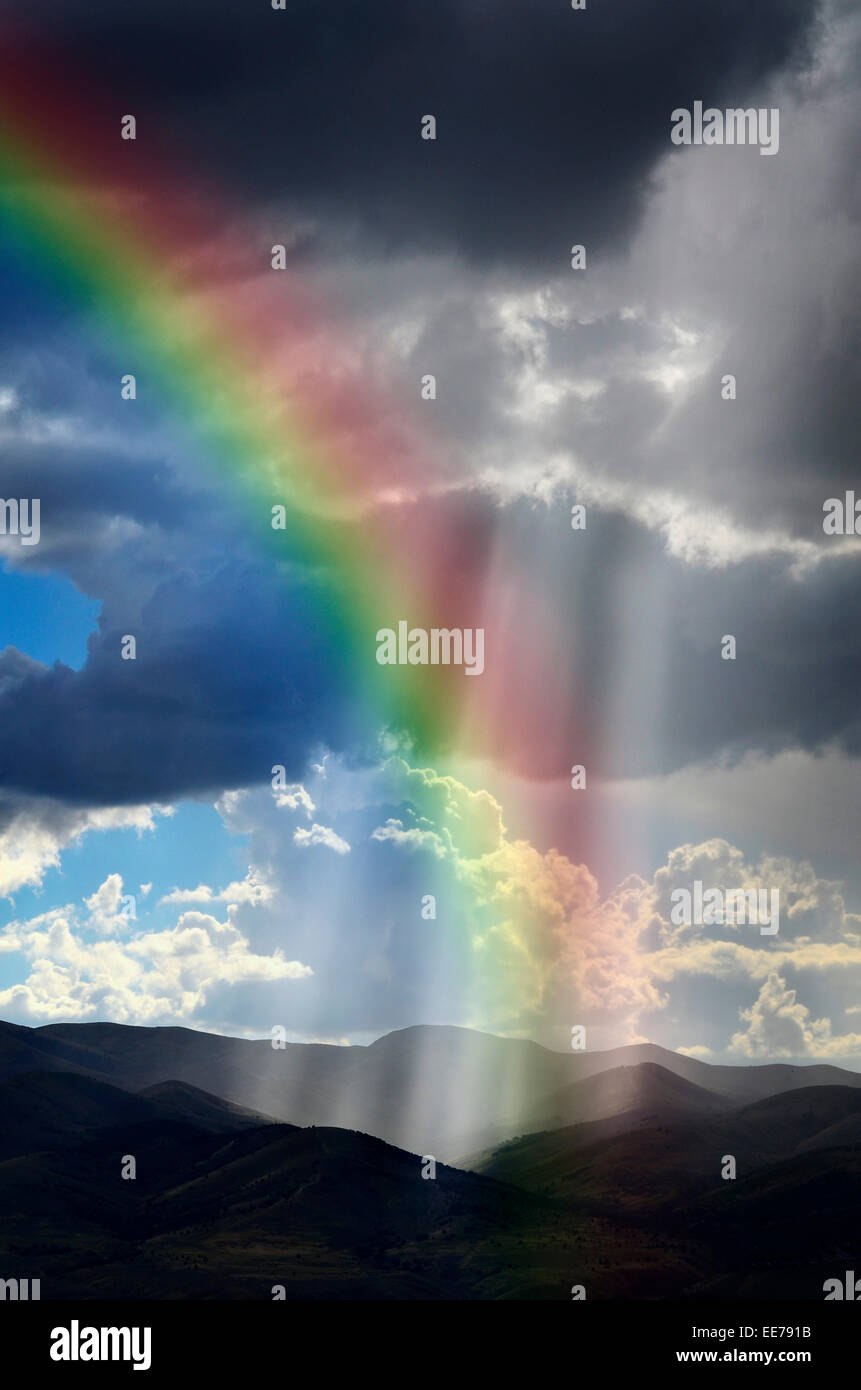 Sunlight rays from clouds falling on dark mountain range with Rainbow ...