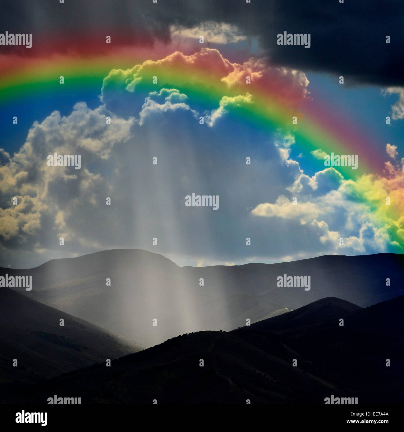 Sunlight rays from clouds falling on dark mountain range with Rainbow ...