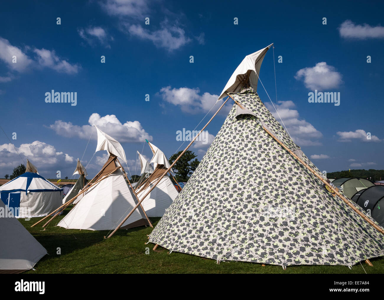 Several tipi tents at a festival in the UK against a blue sky with ...