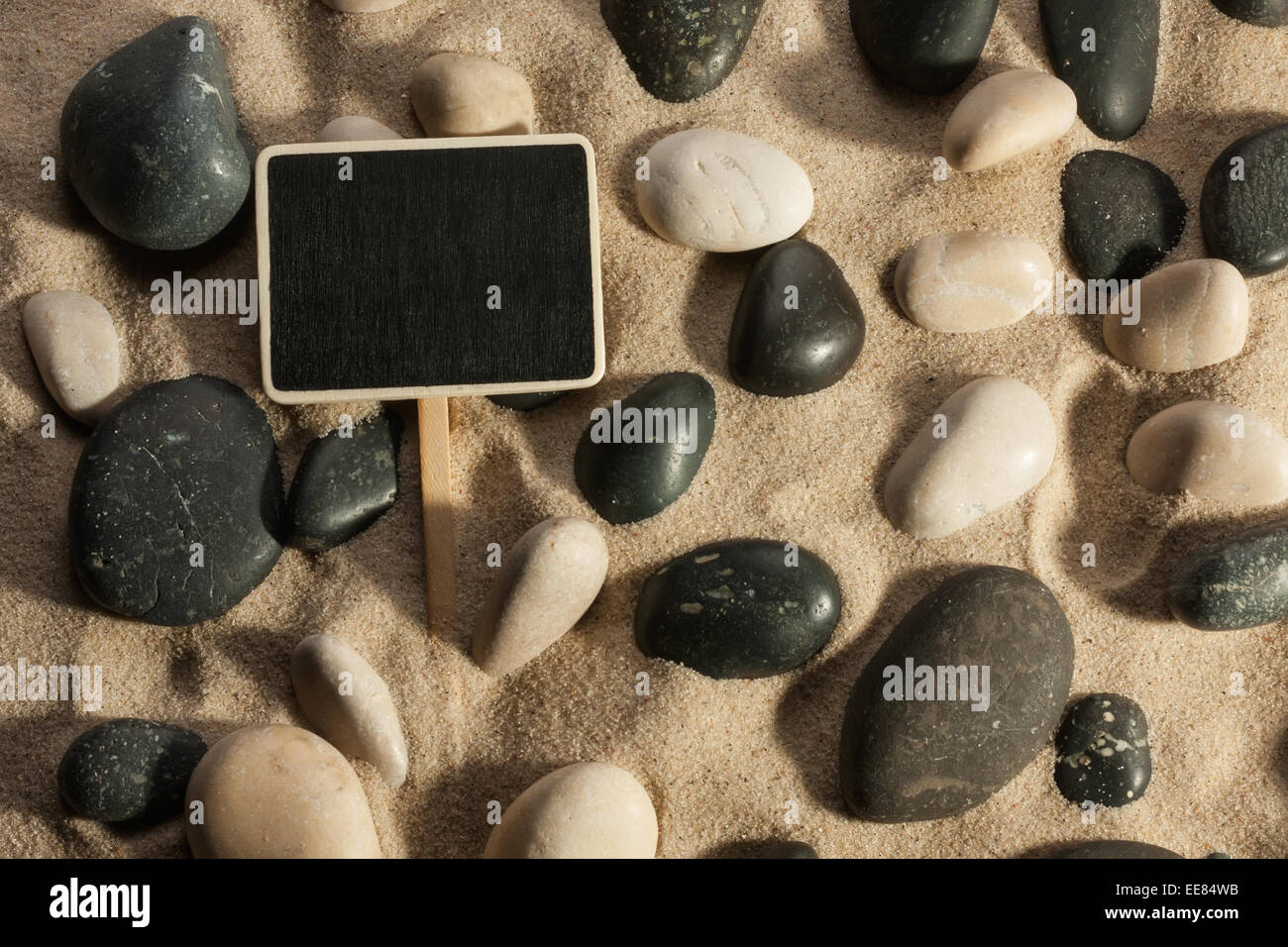 Close-up of stones and sign sticking out of the sand in the sunlight ...