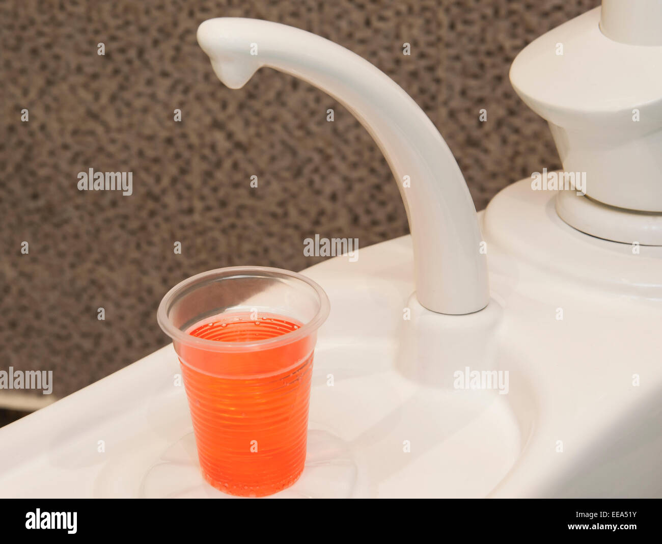Closeup detail of orange mouthwash drink and faucet in dentists surgery ...