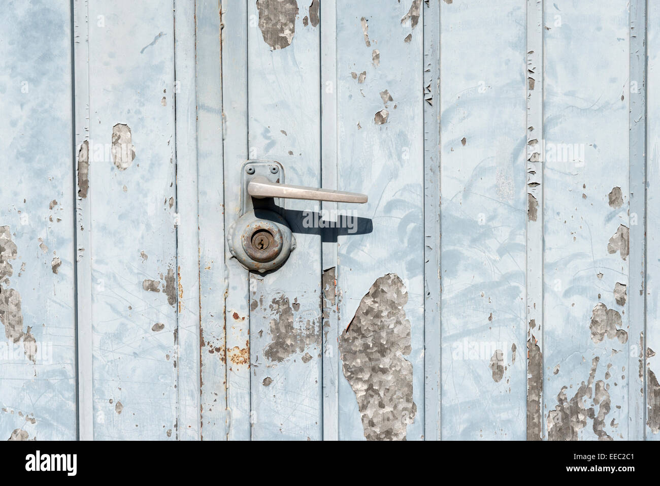 An old blue metal door showing the handle and lock with peeling paint ...