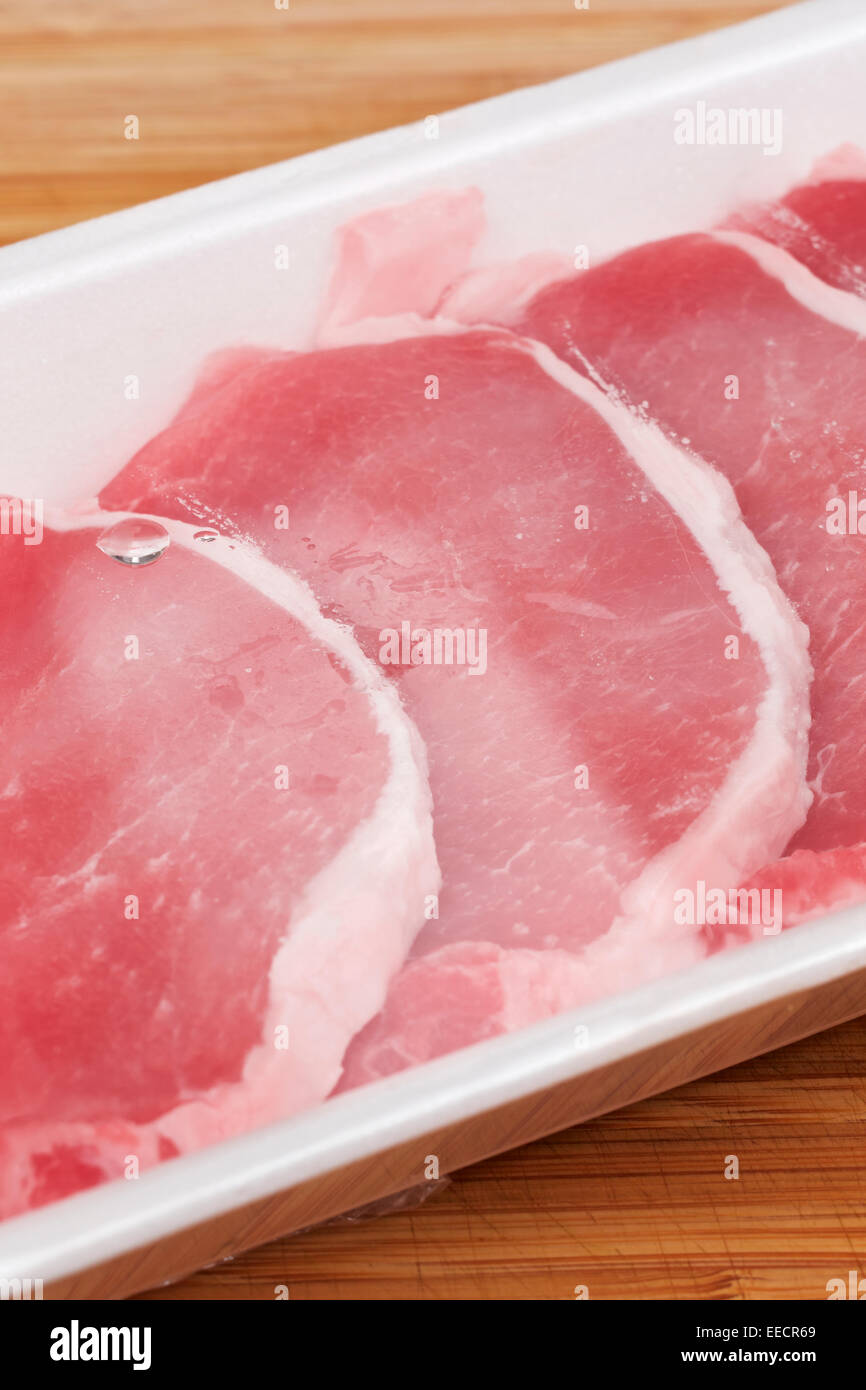 Packaged pork chops from the grocery store on a wood cutting board ...
