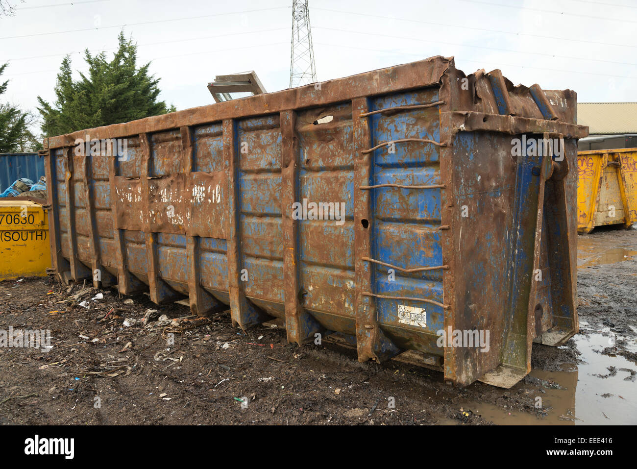 Large rusted metal skip at a wet muddy Industrial estate in winter ...