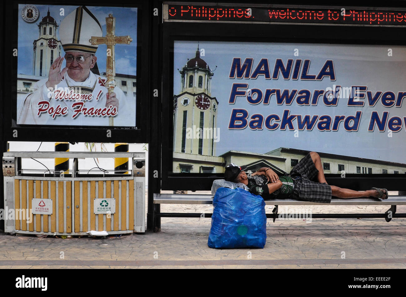 A homeless sleeps in a waiting shed with a Pope Francis display along ...