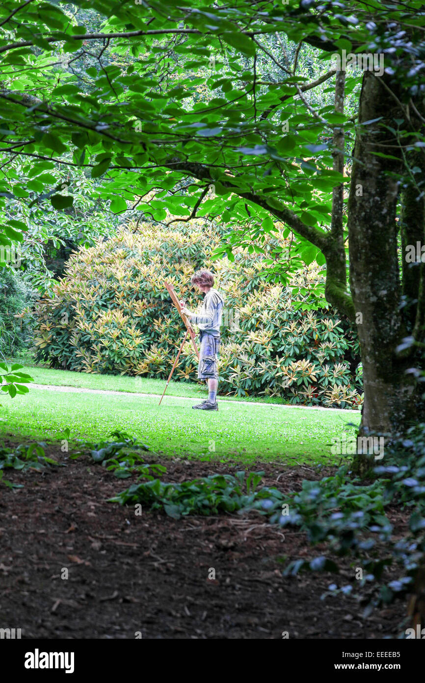 A young man sketching and painting on an easel outside at Trewidden ...