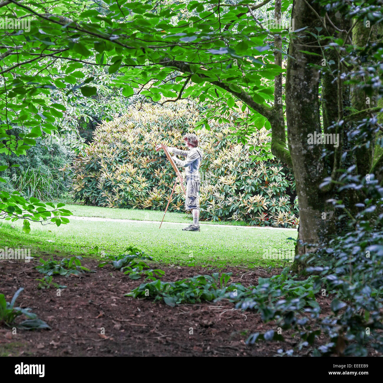 A young man sketching and painting on an easel outside at Trewidden ...