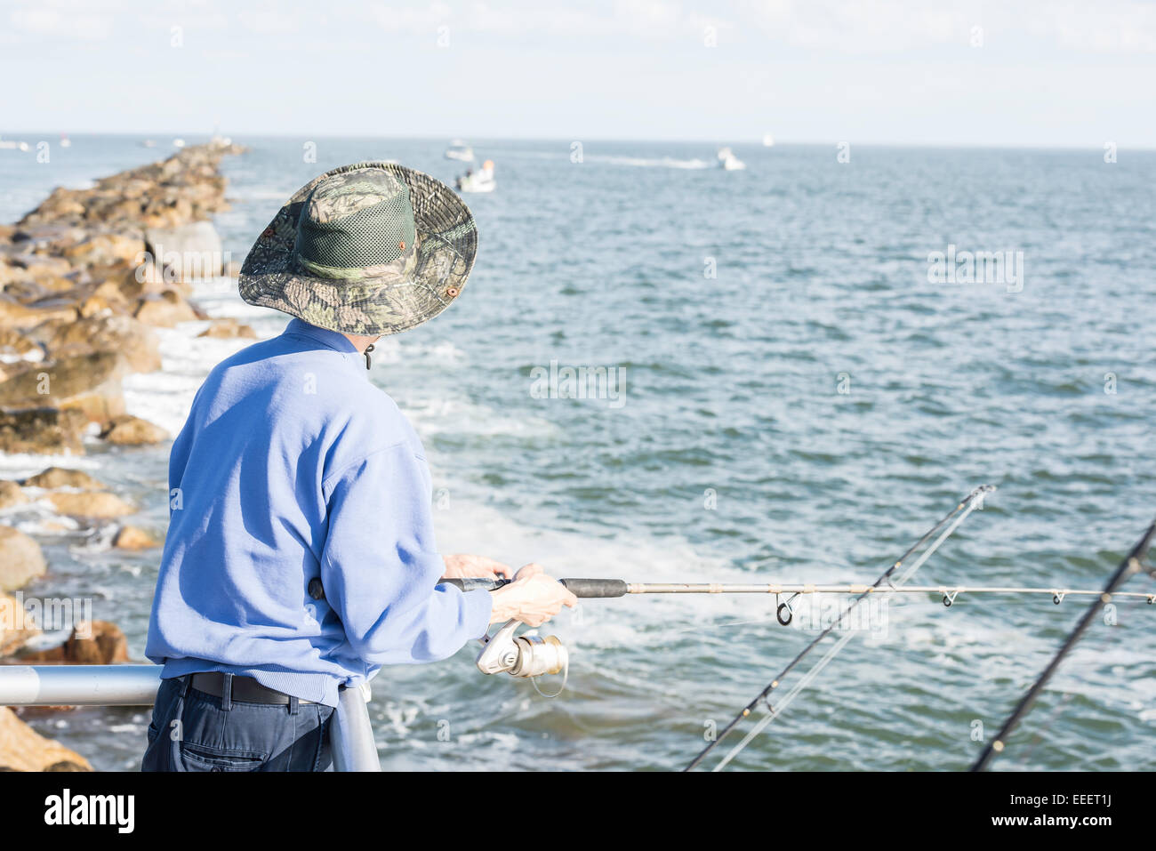 Man with sun hat seen from back standing at a railing with fishing rod ...