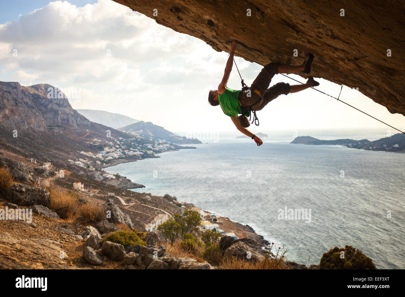 Male rock climber climbing along a roof in a cave at sunset Stock Photo ...
