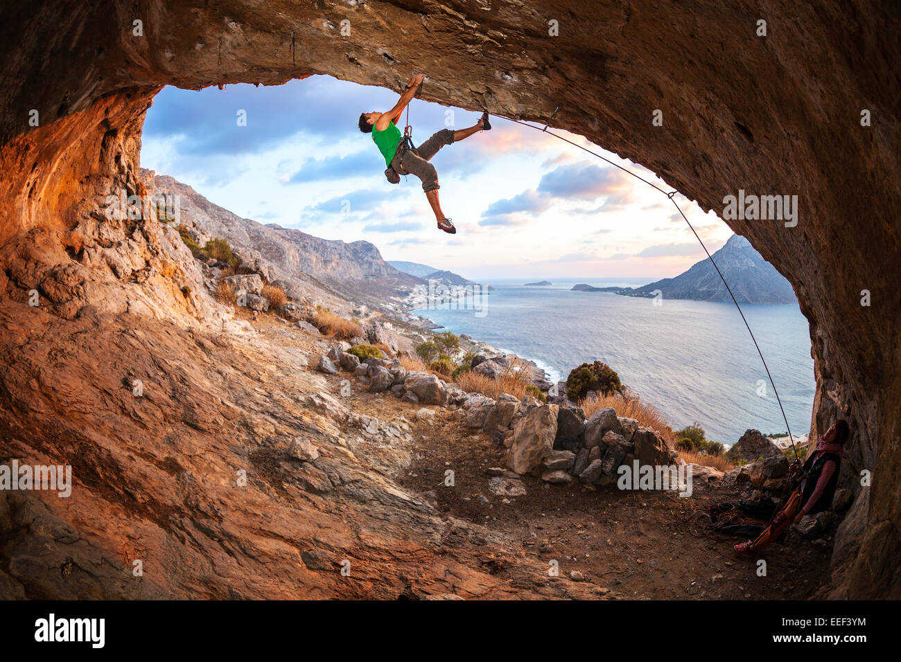 Male rock climber climbing along a roof in a cave at sunset Stock Photo ...