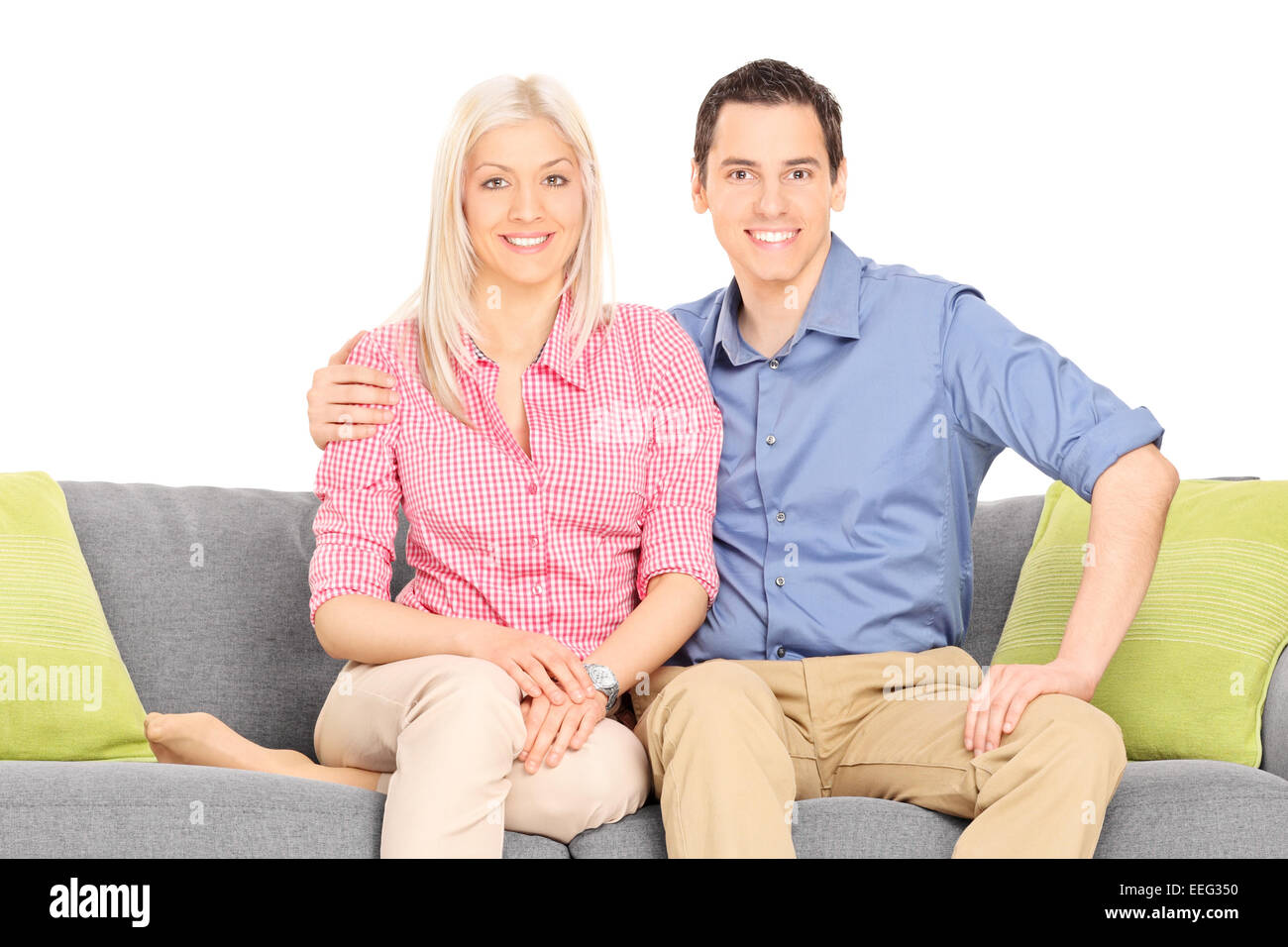 Young couple sitting on a modern sofa isolated against white background ...