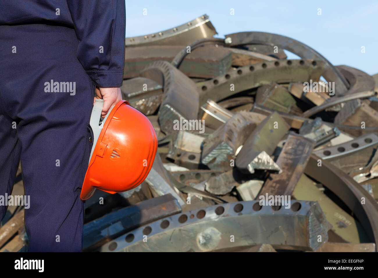 closeup of worker holding helmet standing facing pile of disposed metal ...