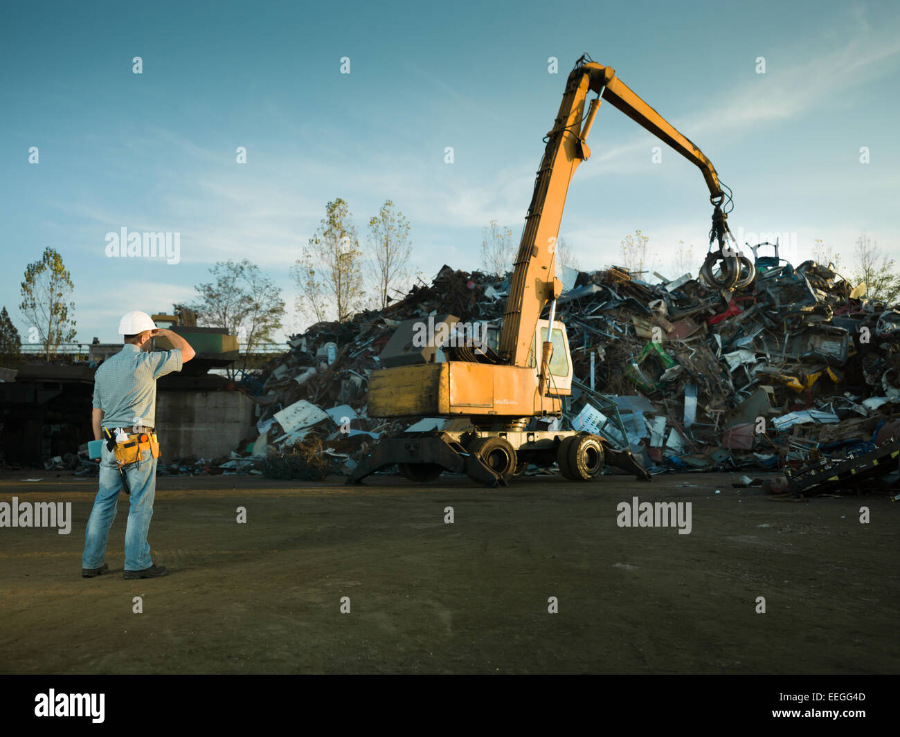 worker standing in recycling landfill looking at scrap metal stack ...
