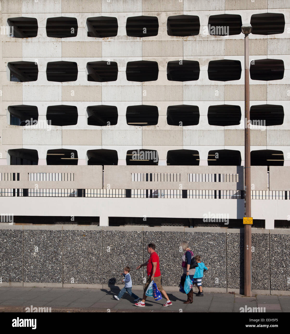 Family group walking past ugly multi-storey car park (ramp) at Worthing ...