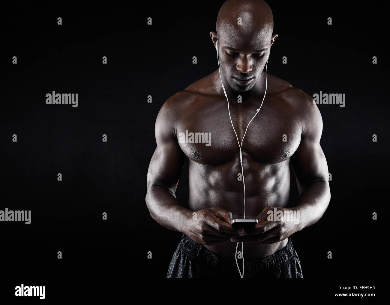 Studio shot of muscular young man listening music on mobile phone ...