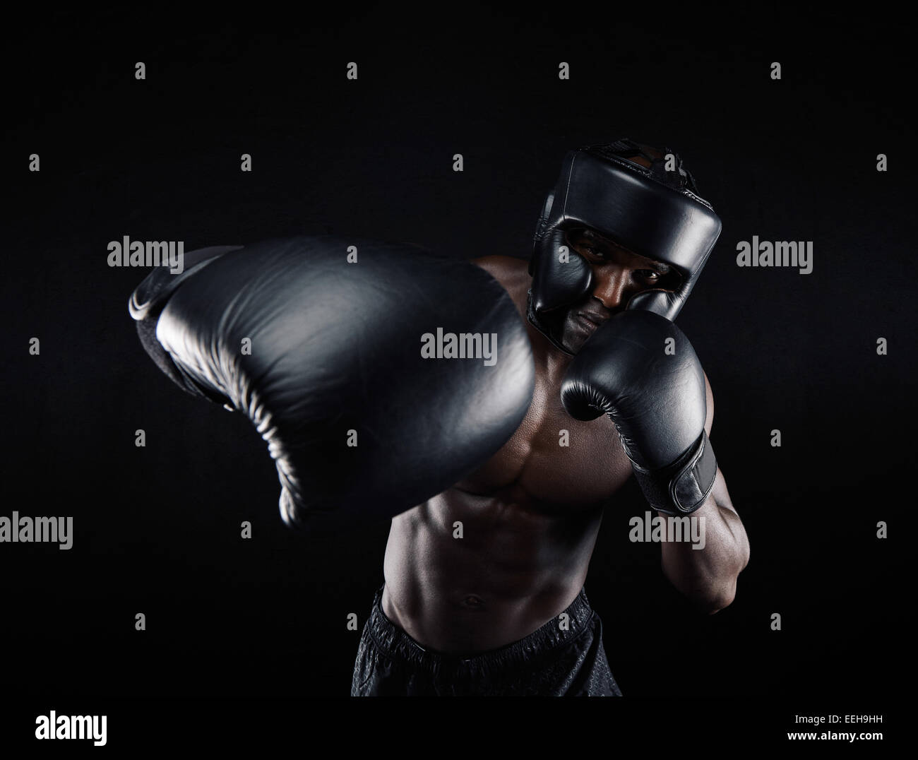 Portrait of African male practicing boxing against black background ...