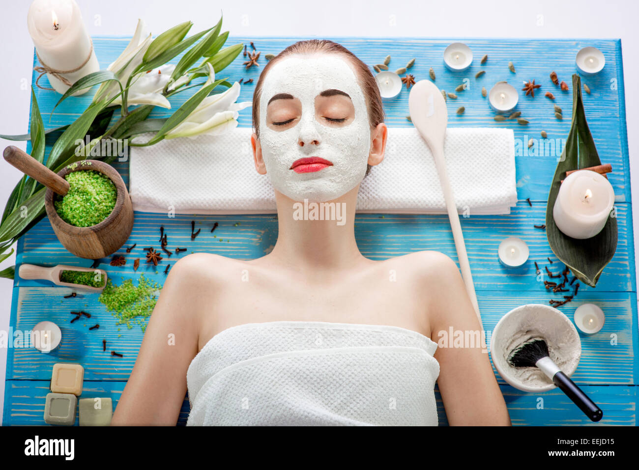 Young woman with spa facial mask on her face lying on blue table with ...
