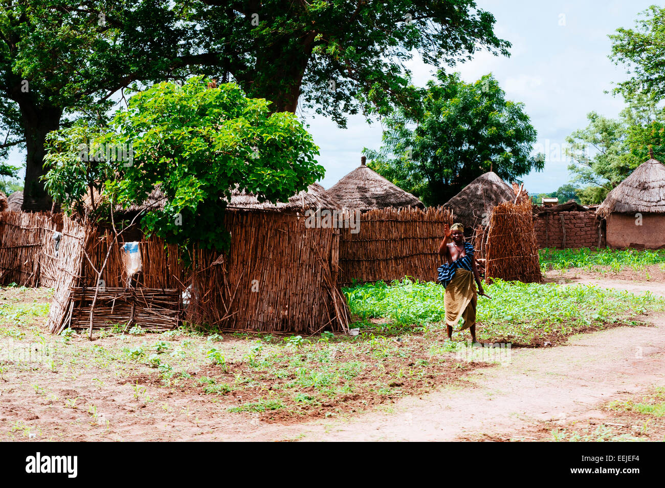 Woman saying hello in her mud brick and thatched roof huts village ...