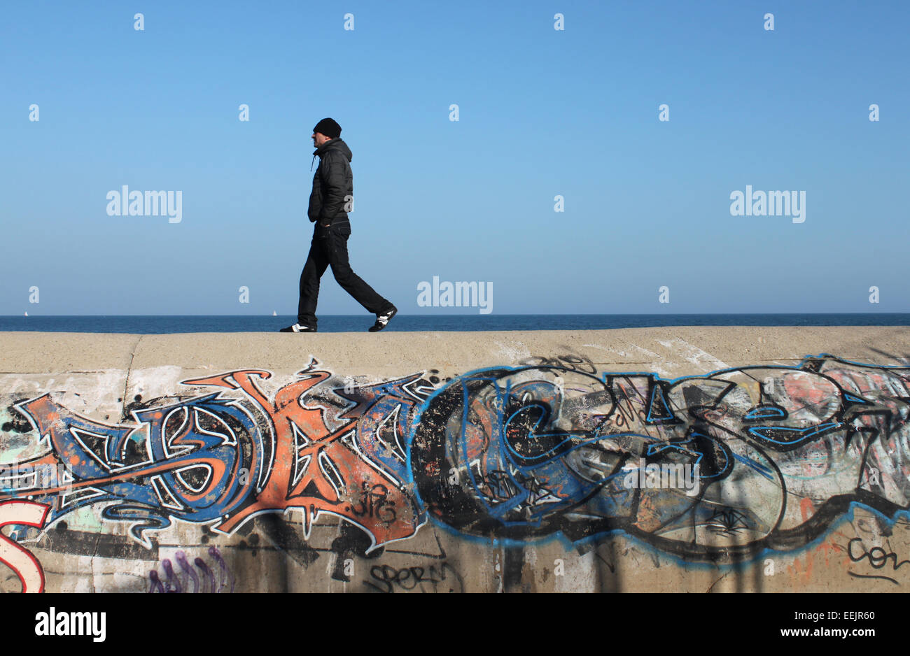 Man walking along graffiti covered wall next to sea, near Badalona ...