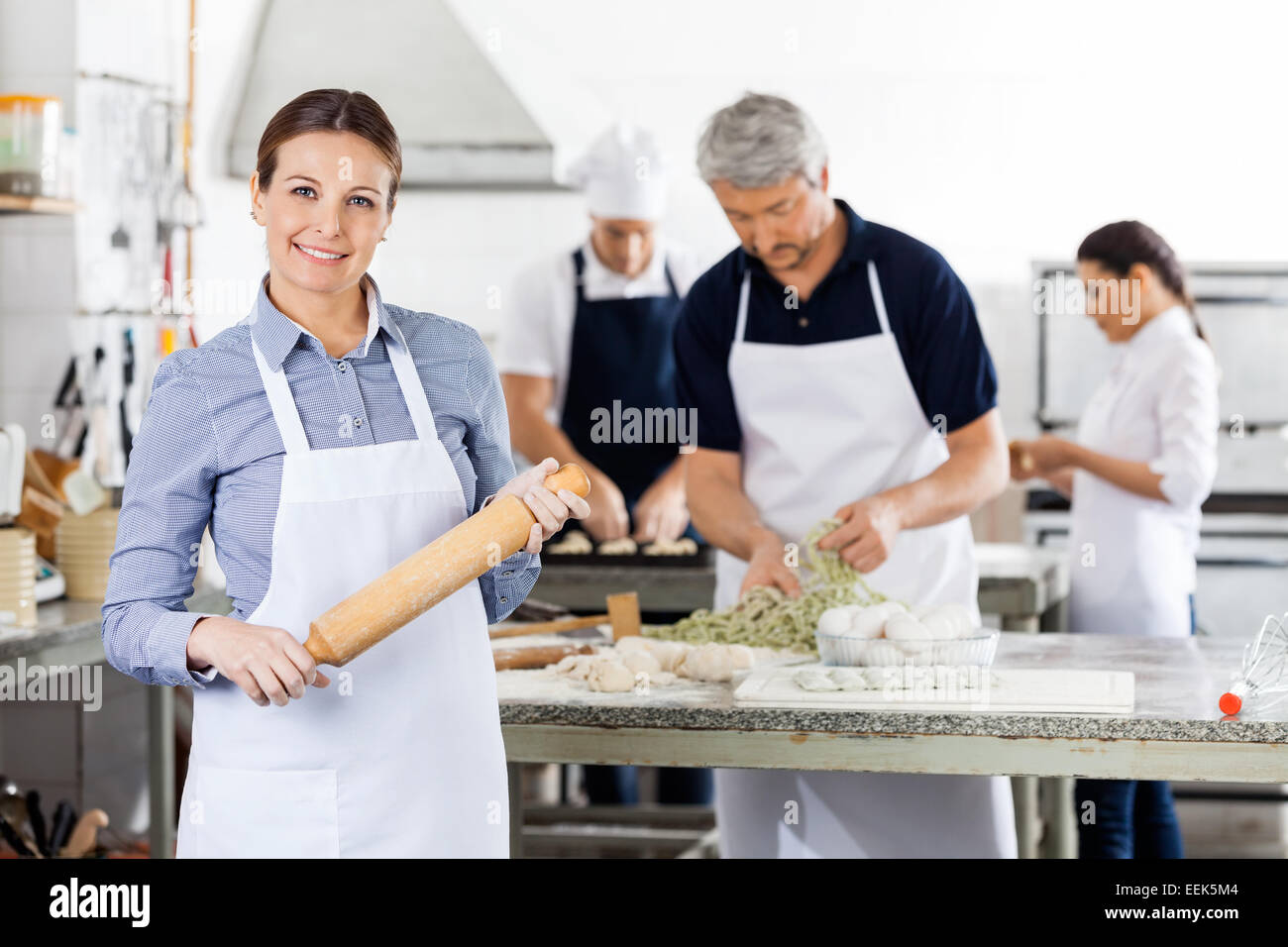 Confident Female Chef Holding Rolling Pin While Colleagues Prepa Stock ...