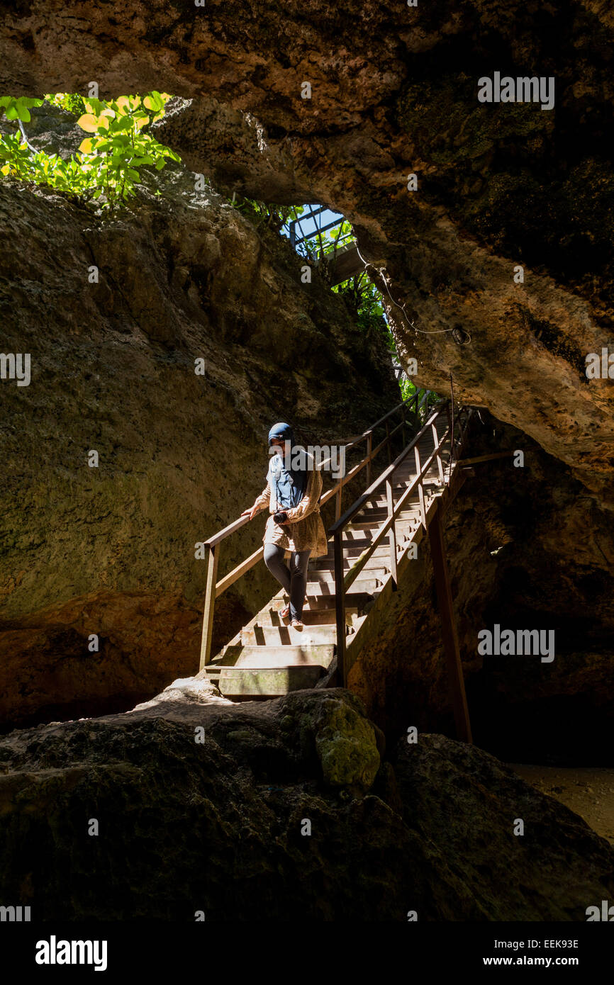 Woman walking down a stairway through a cave to get to Padang Padang ...