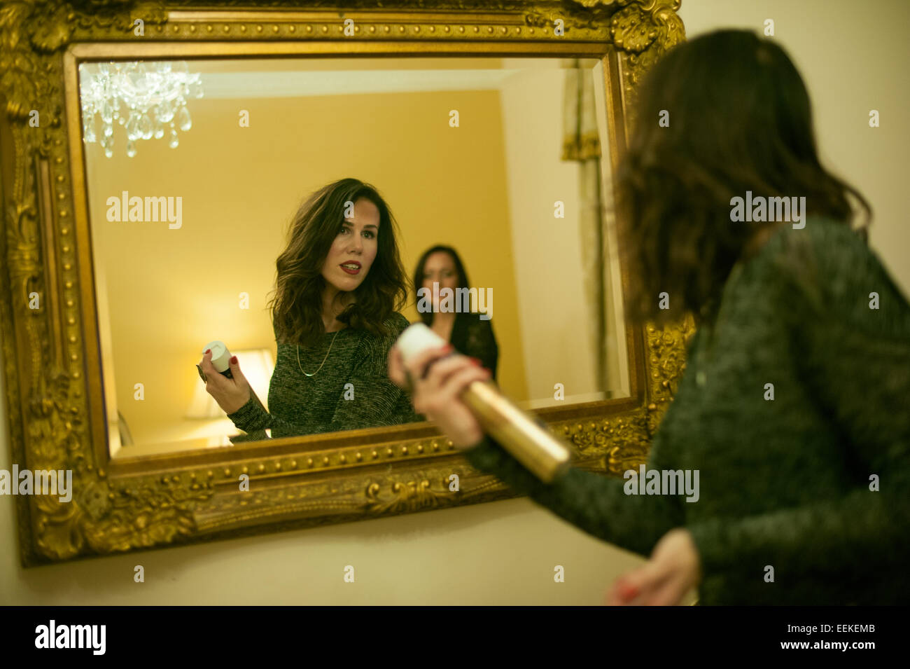 Woman getting ready for a night out looking at herself in a large gilt ...