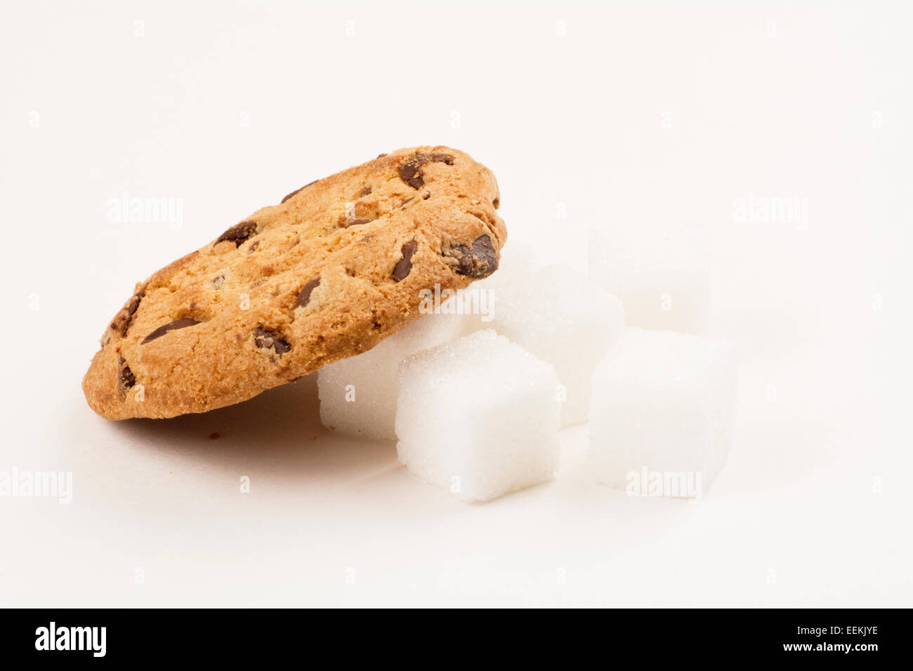 A chocolate chip cookie with several sugar cubes under and beside it ...