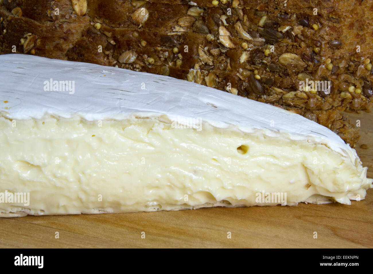 Wedge of brie cheese on wooden cutting board with loaf of whole grain ...