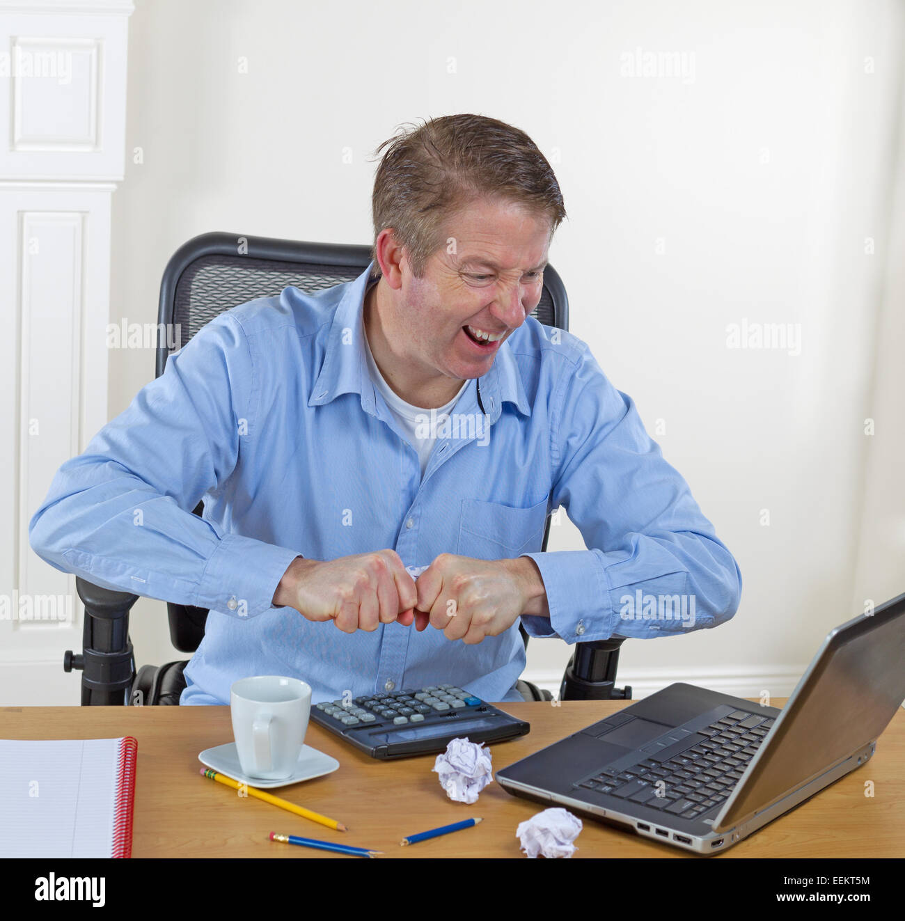 Mature man ripping paper while looking down at desktop with laptop ...