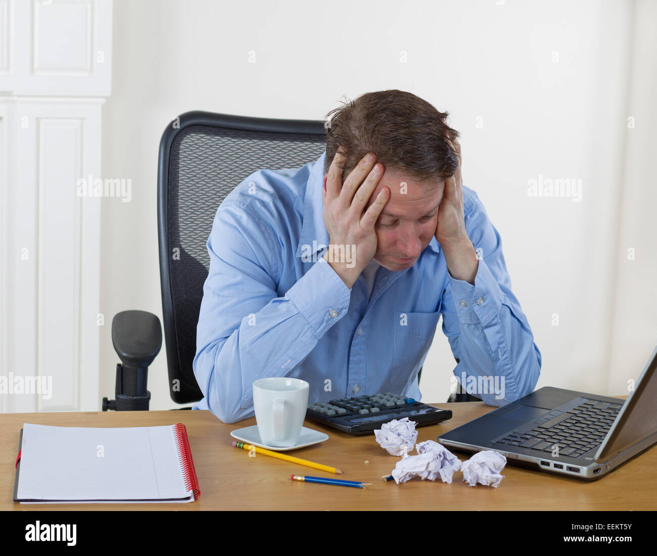 Mature man holding head in his hands while looking down at desktop with ...