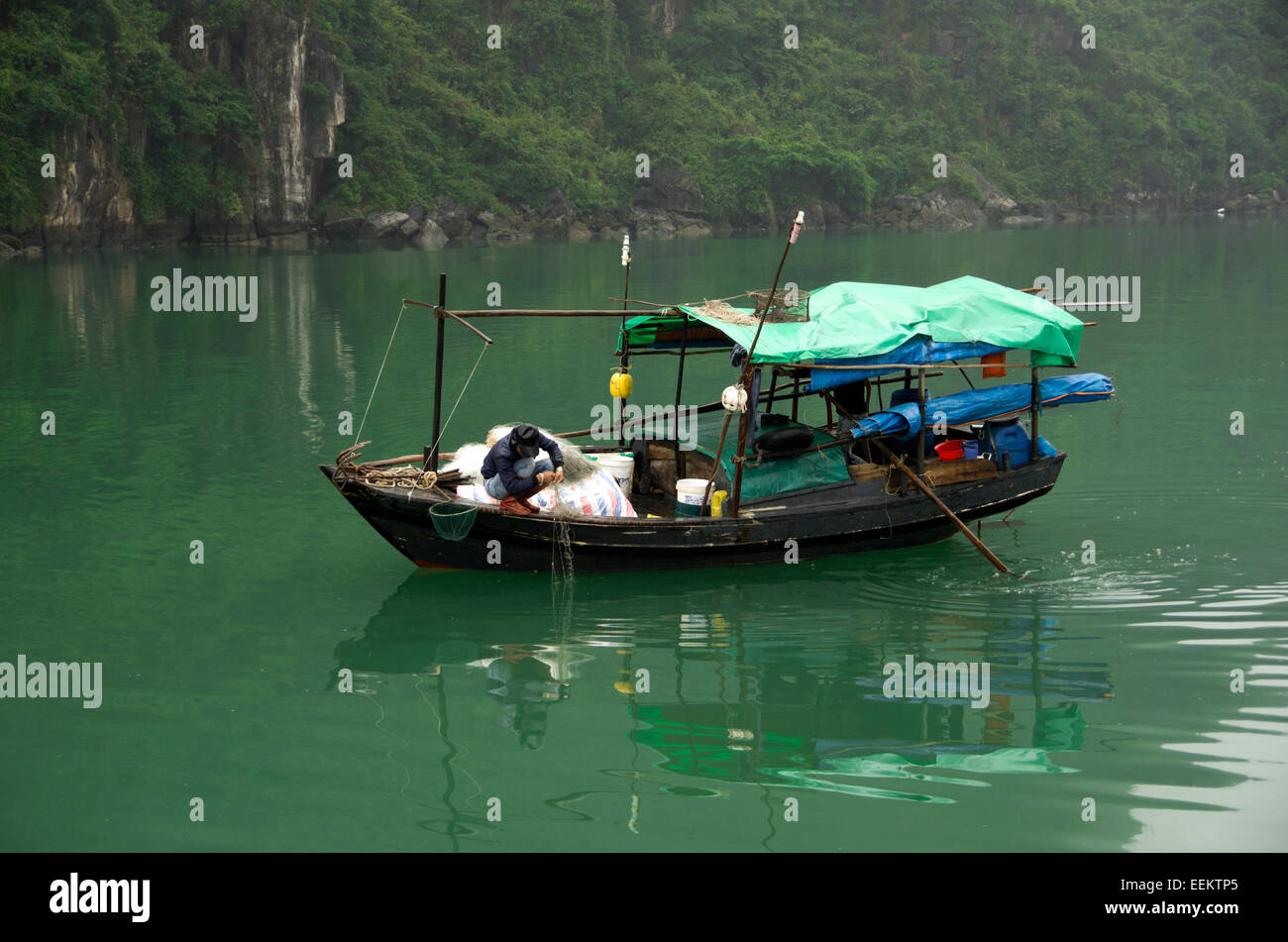 Fisherman hangs his net over the side of small colorful boat, helmsman ...