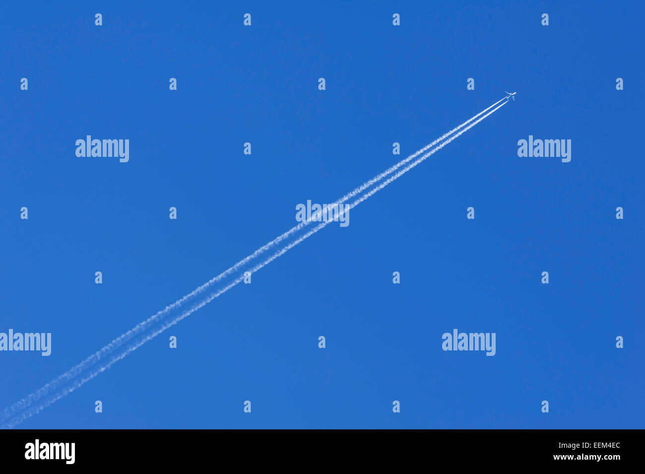 Plane with contrails against a blue sky Stock Photo - Alamy