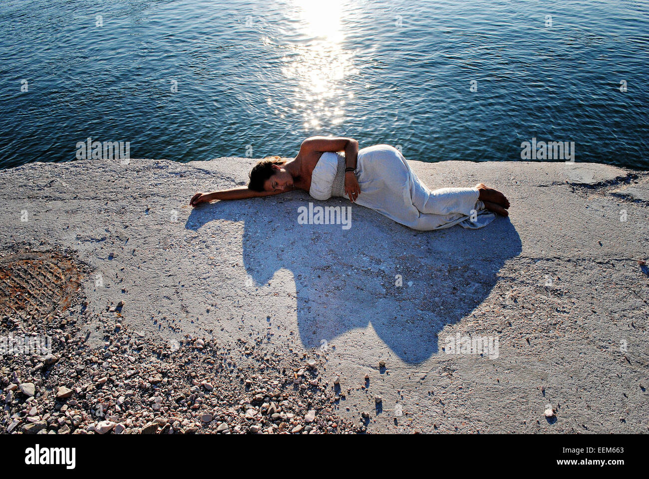 Young woman laying on rock by sea Stock Photo - Alamy