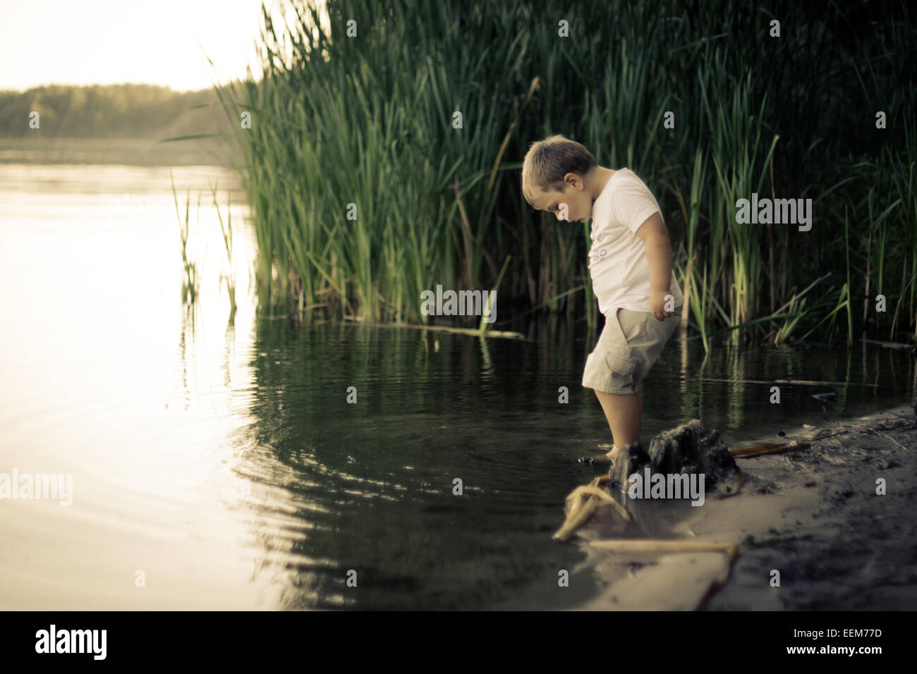 Portrait of boy testing the water of calm pond with leg Stock Photo - Alamy