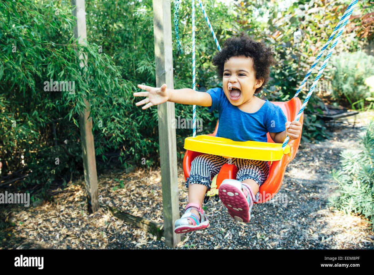 Low angle view of mixed race girl shouting on swing Stock Photo - Alamy