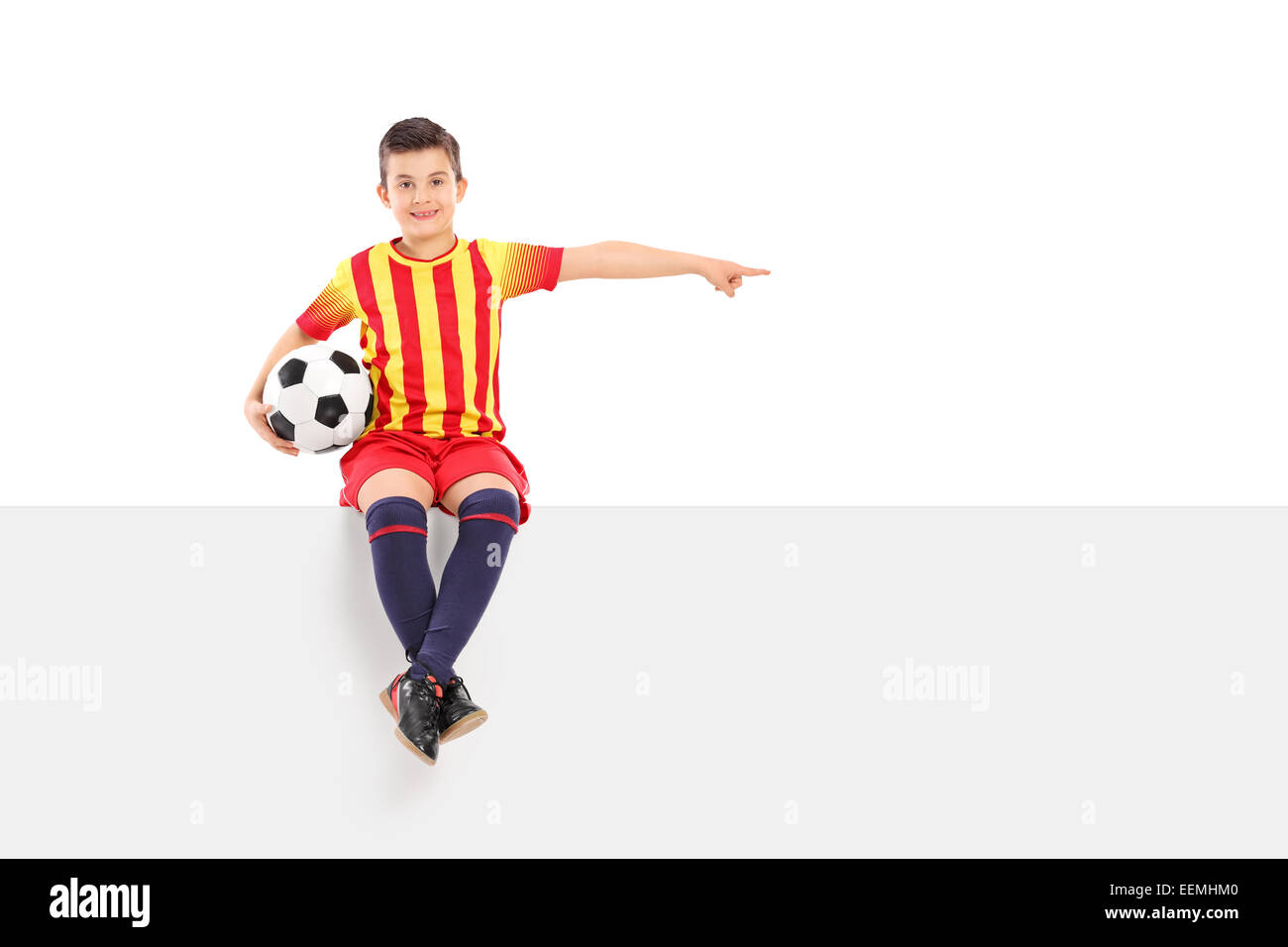 Junior football player pointing with his hand seated on panel isolated ...