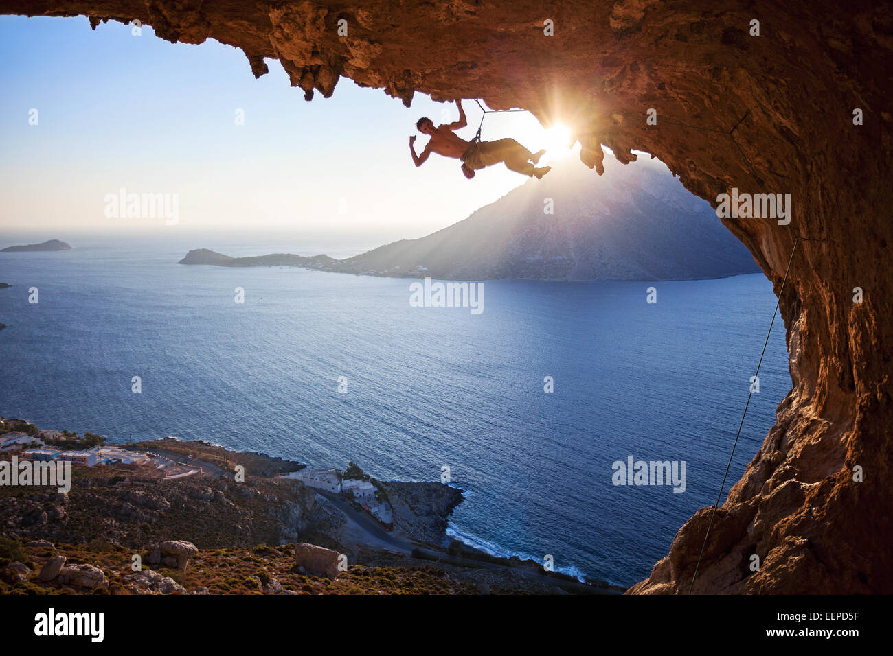 Male rock climber flexing his bicep while hanging on one arm at sunset ...