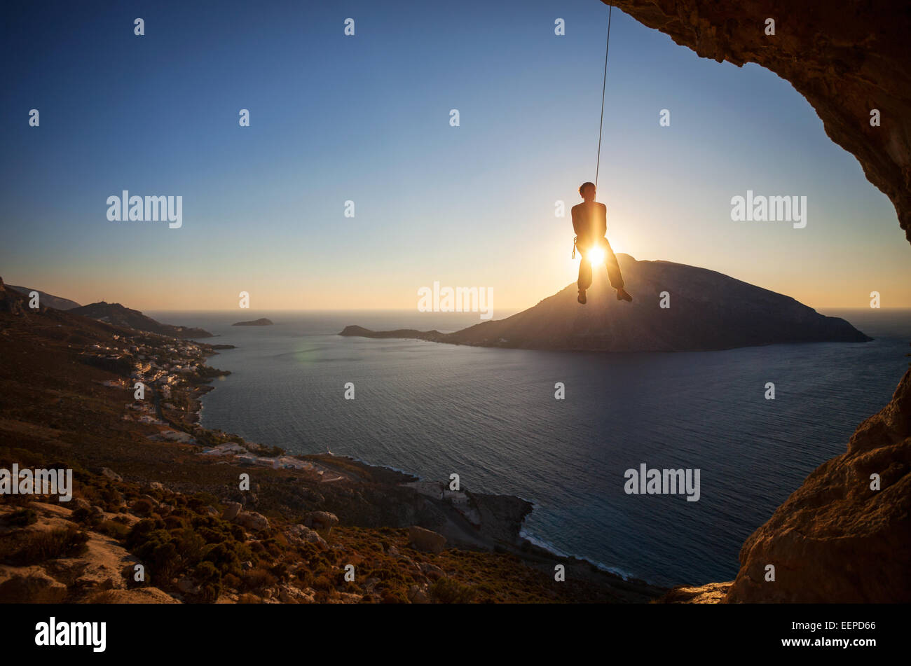 Rock climber hanging on rope while lead climbing at sunset, with ...