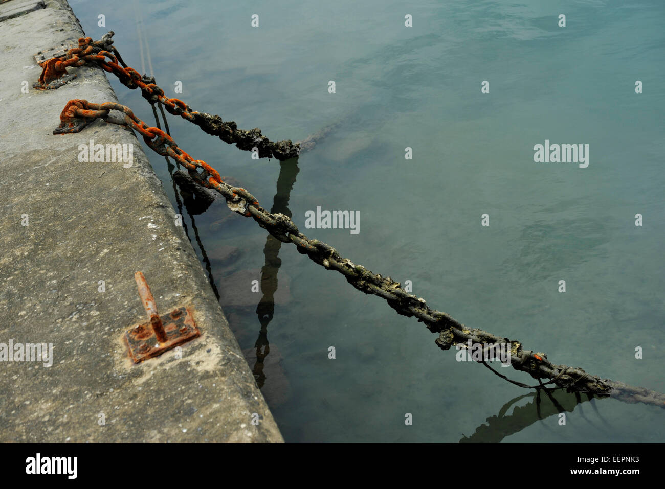 Atmospheric scene of two rusty dirty chains secured to dock side ...