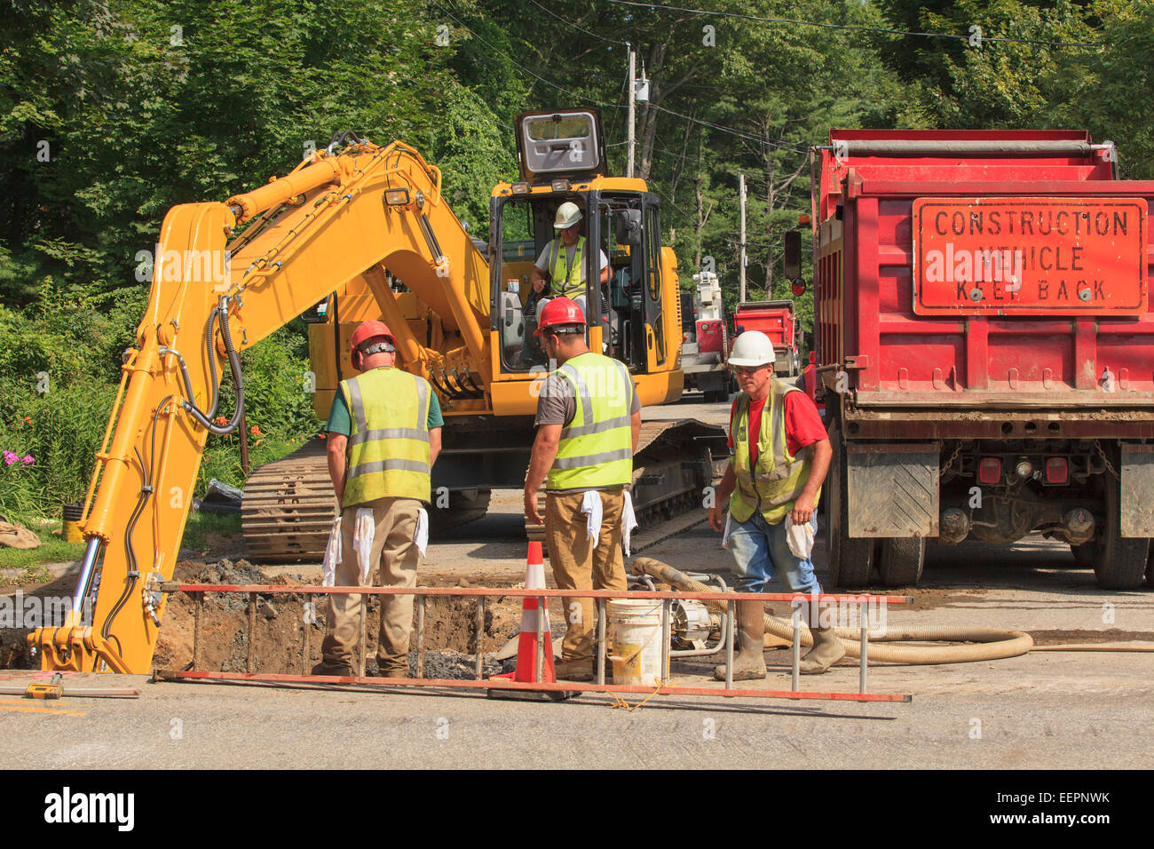 Construction workers watching excavators digging hole on watermain ...