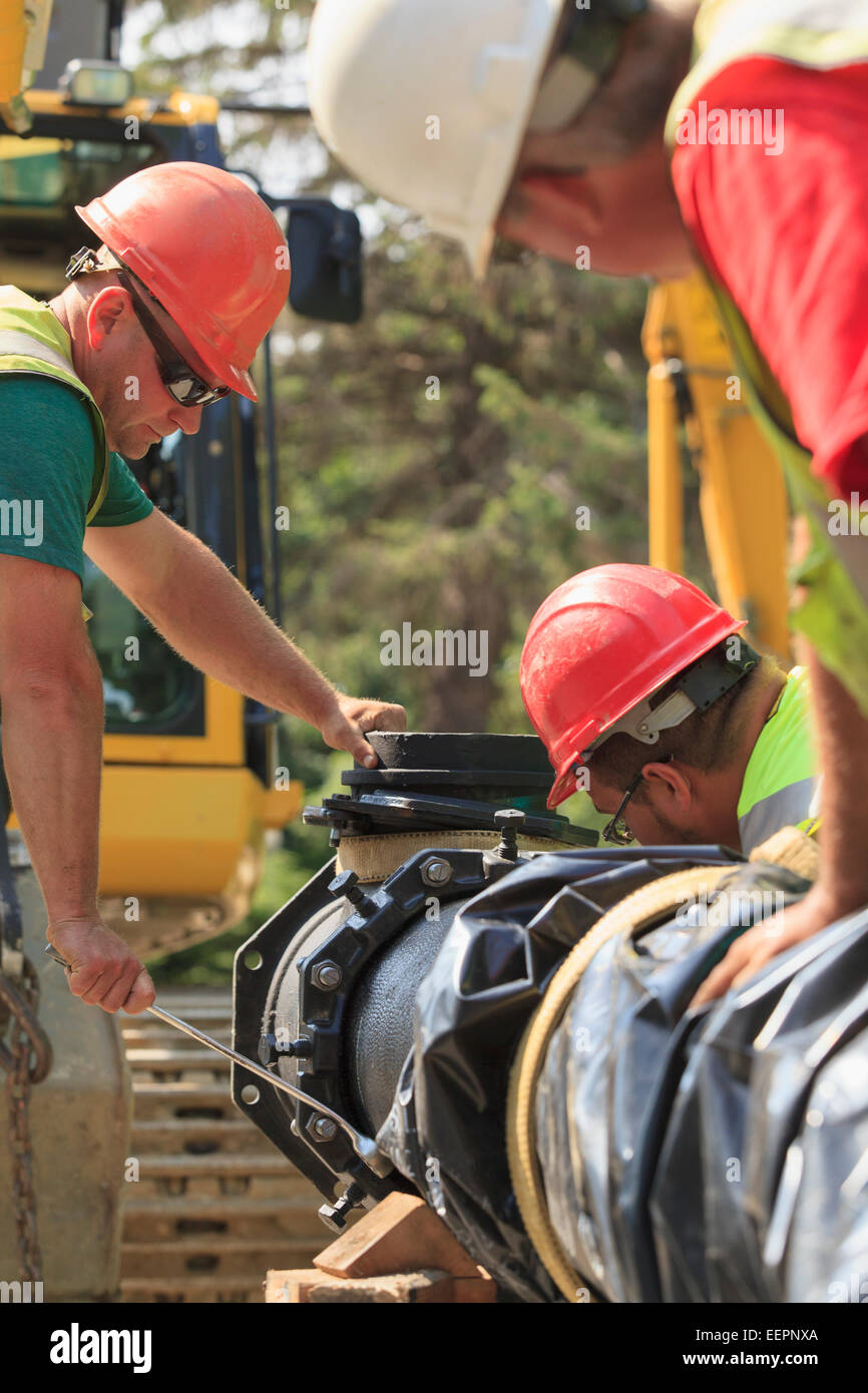 Construction workers using hand wrench to secure water main section ...