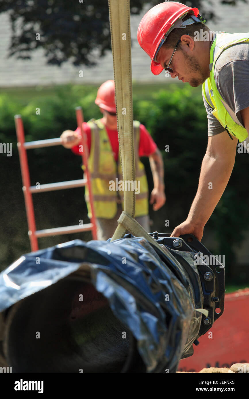 Construction worker using strap on excavator to guide water main ...